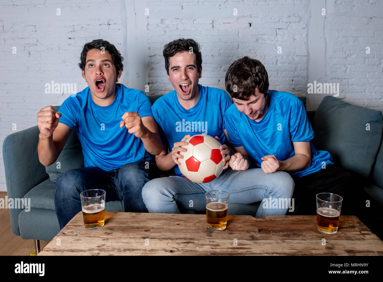 a happy and excited young group of football fans sitting on the sofa ...