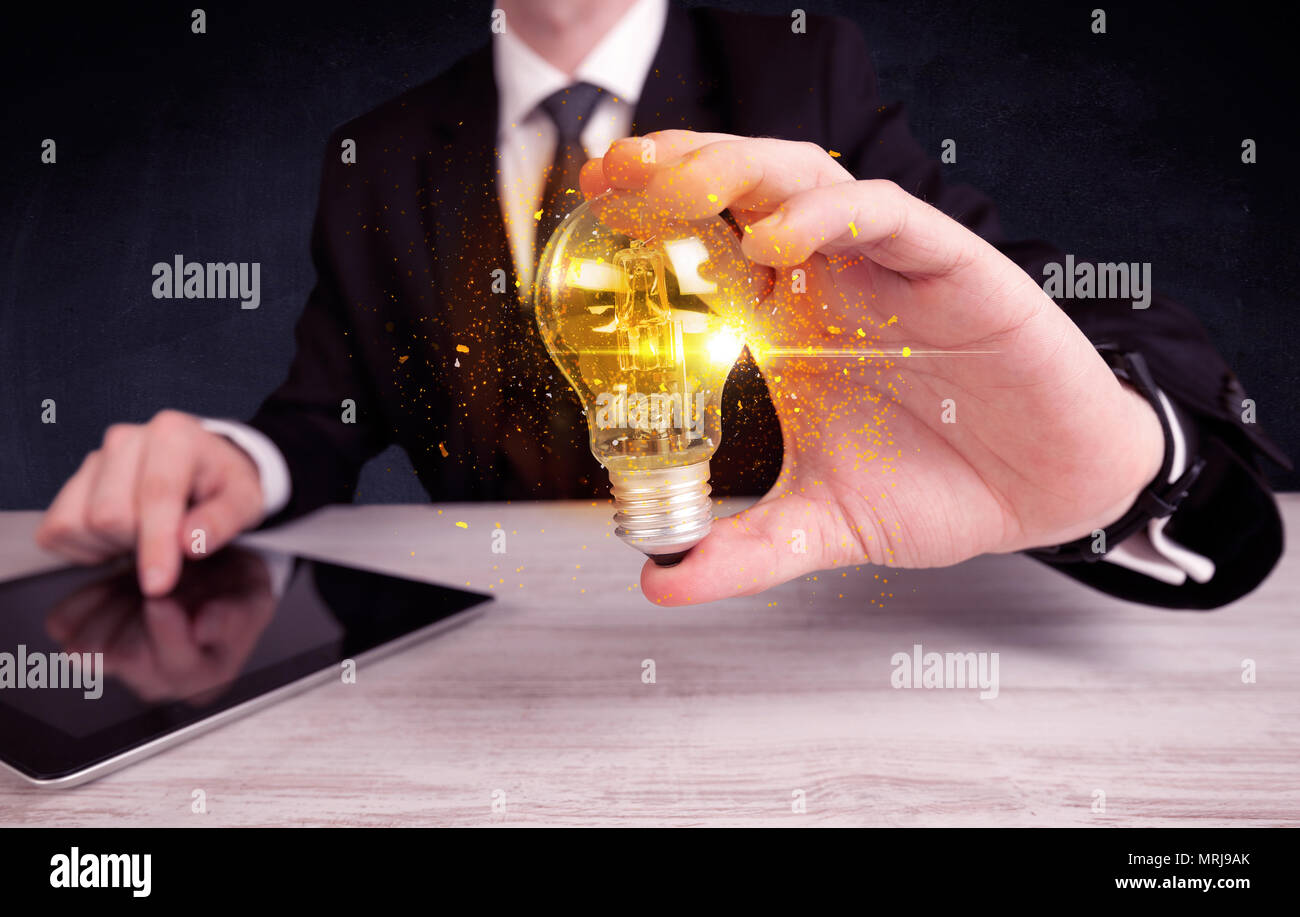 An elegant office worker holding a yellow sparkling light bulb in his ...