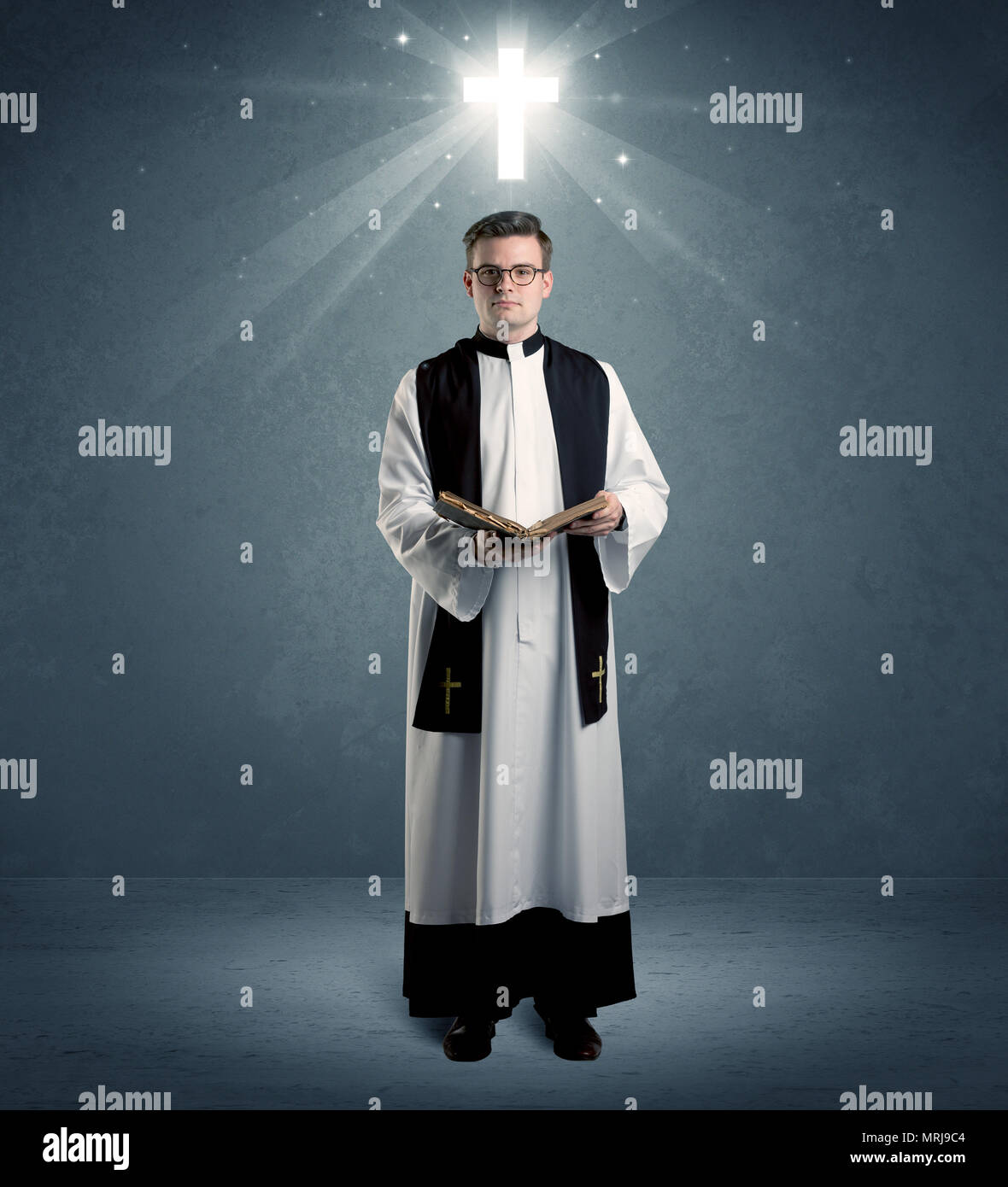 A young caucasian priest with deep faith blessing with the holy bible ...