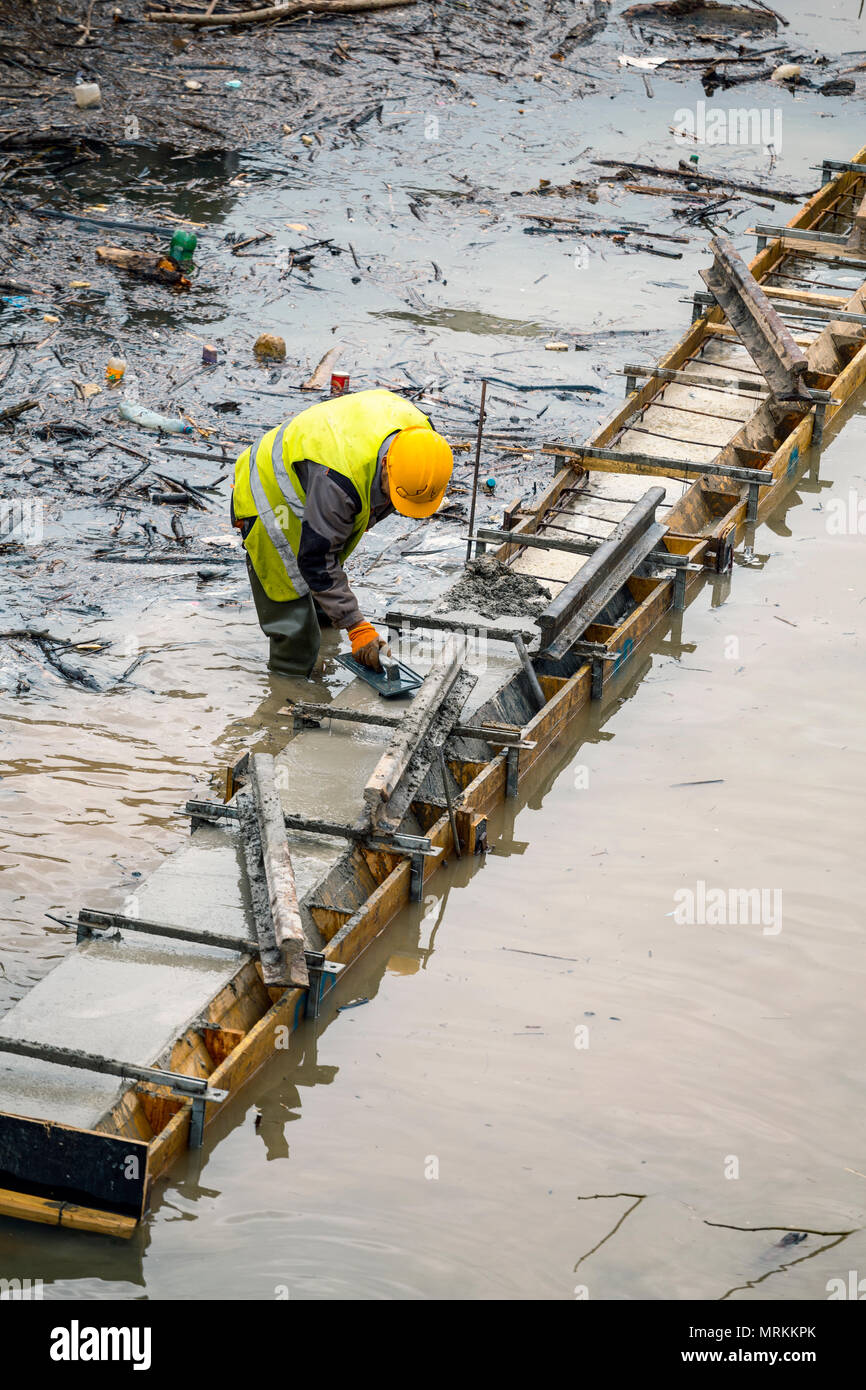 Construction worker leveling concrete formwork in water for river bank ...