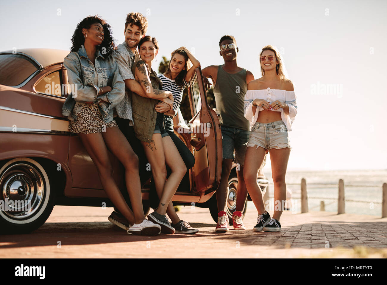 Group of young people on road trip standing by the car. Diverse group ...