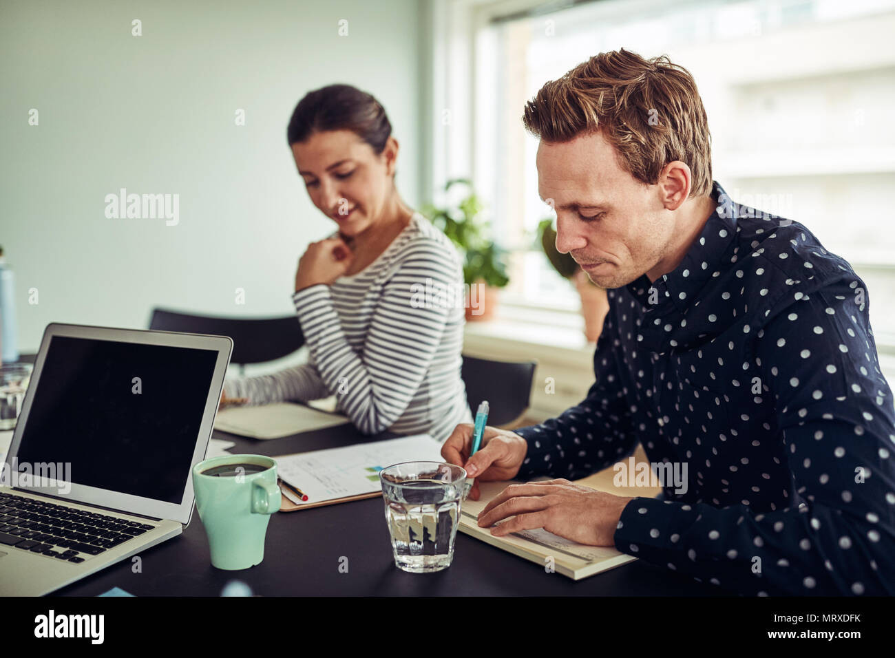 Two smiling young businesspeople sitting together at a desk in a modern ...