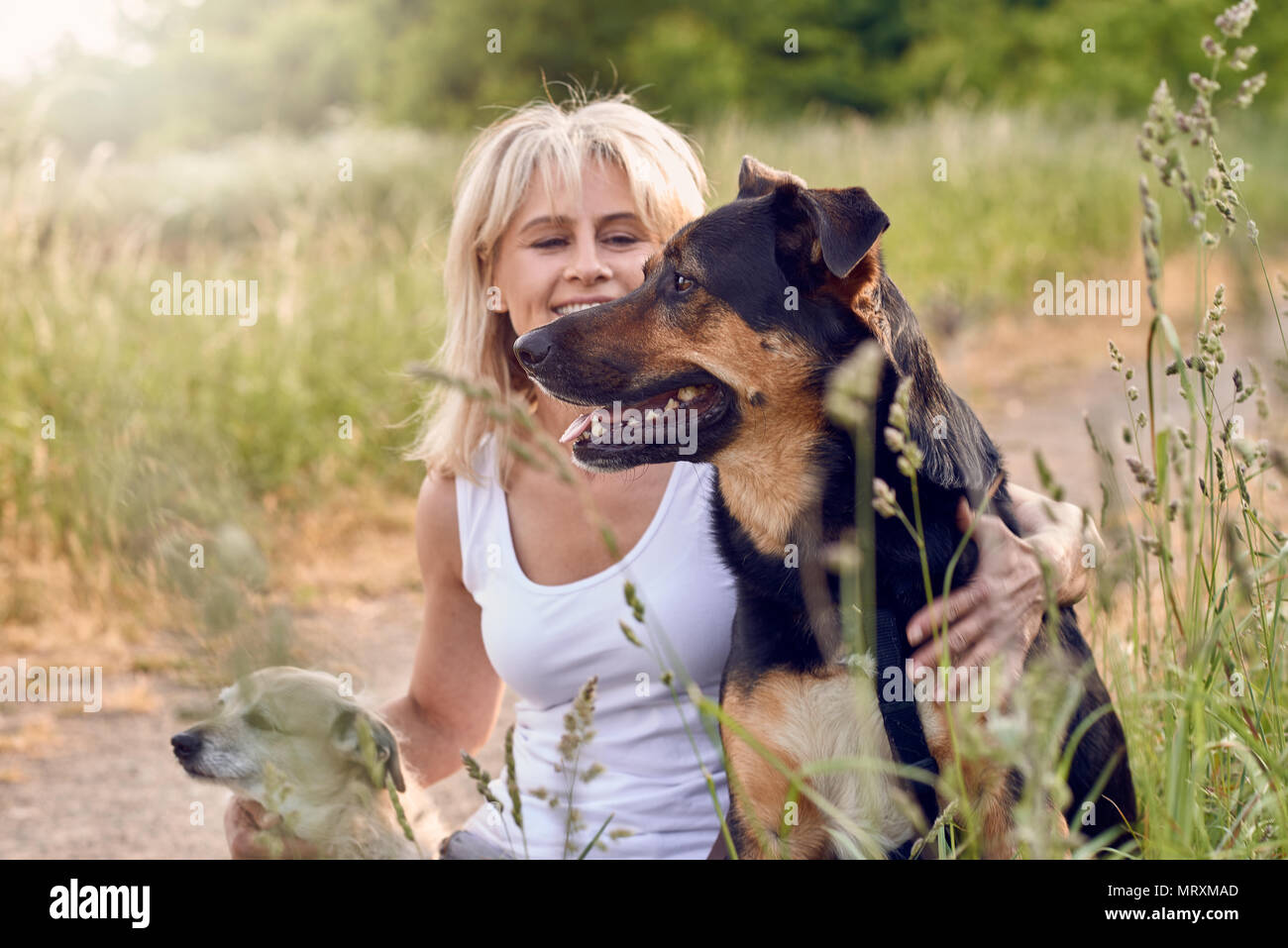 Pretty blond woman with her two dogs crouching with an arm around each ...