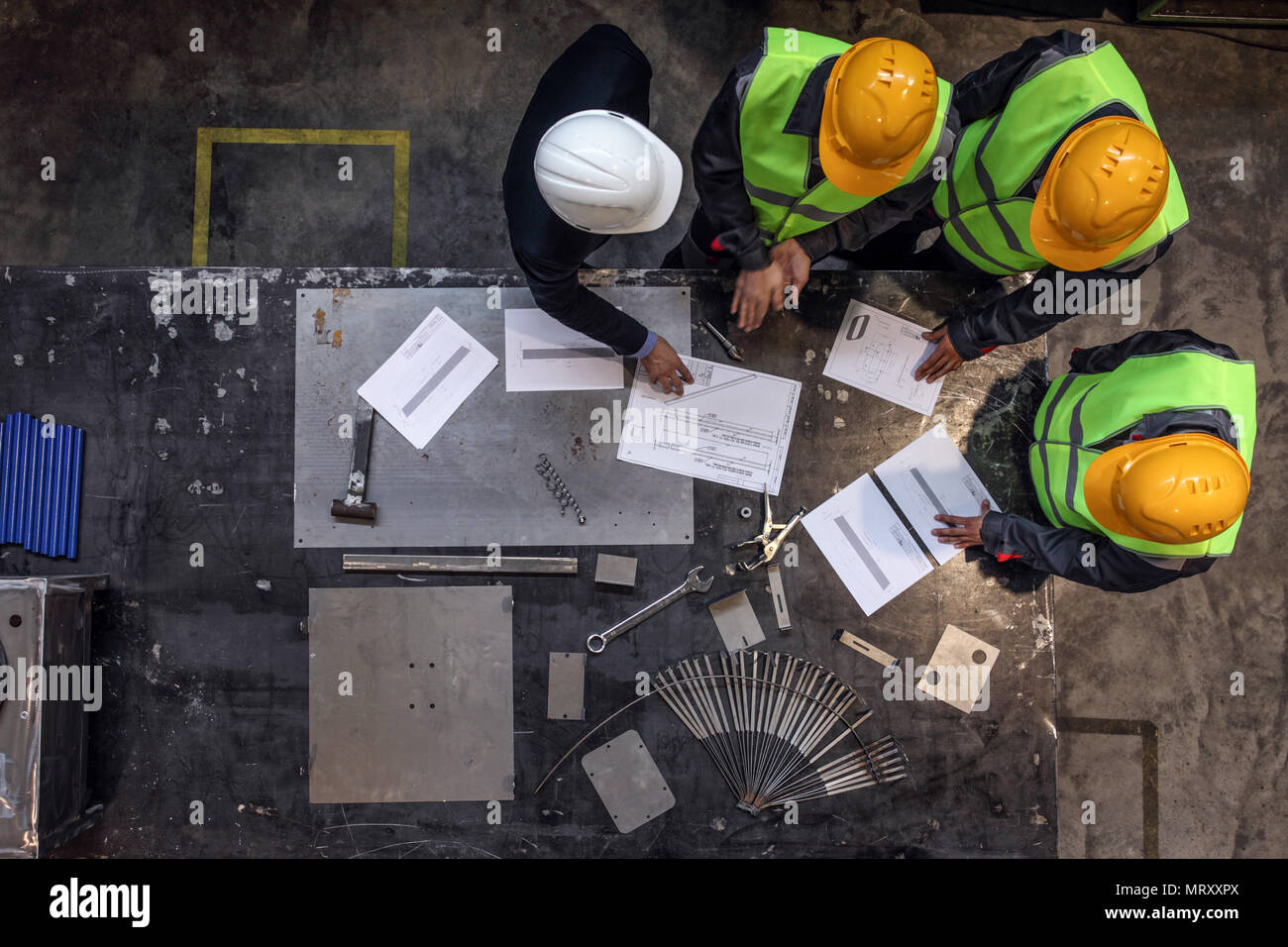 Workers and manager in safety helmets working with documents at factory ...
