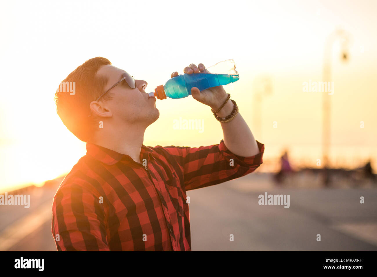 Young man drinking blue isotonic from bottle after hot day on sunset ...