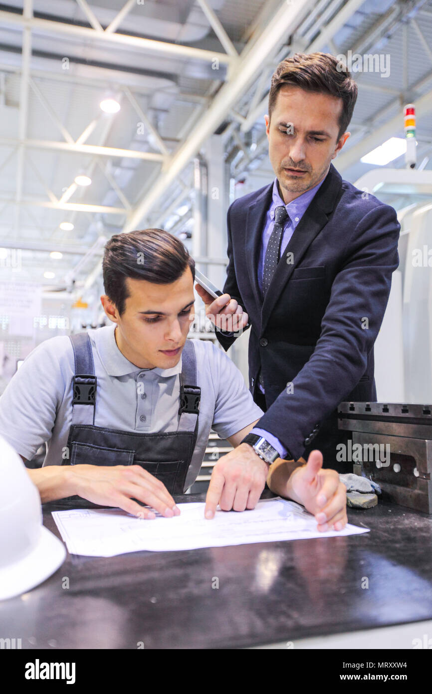Manager and worker working with documents at plant near CNC machines ...