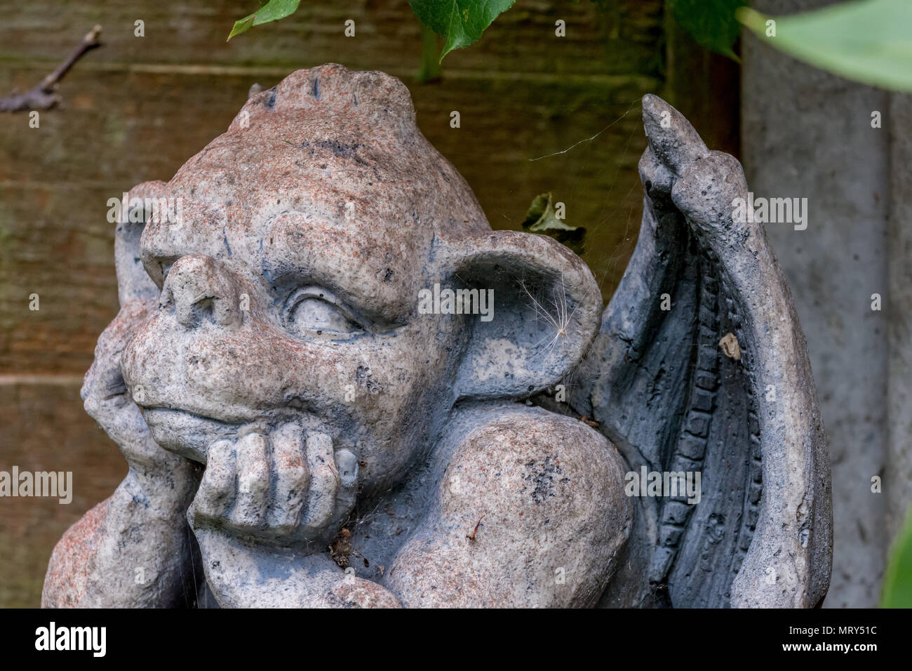 portrait image of garden gargoyle with head in hands and ruefully smile ...