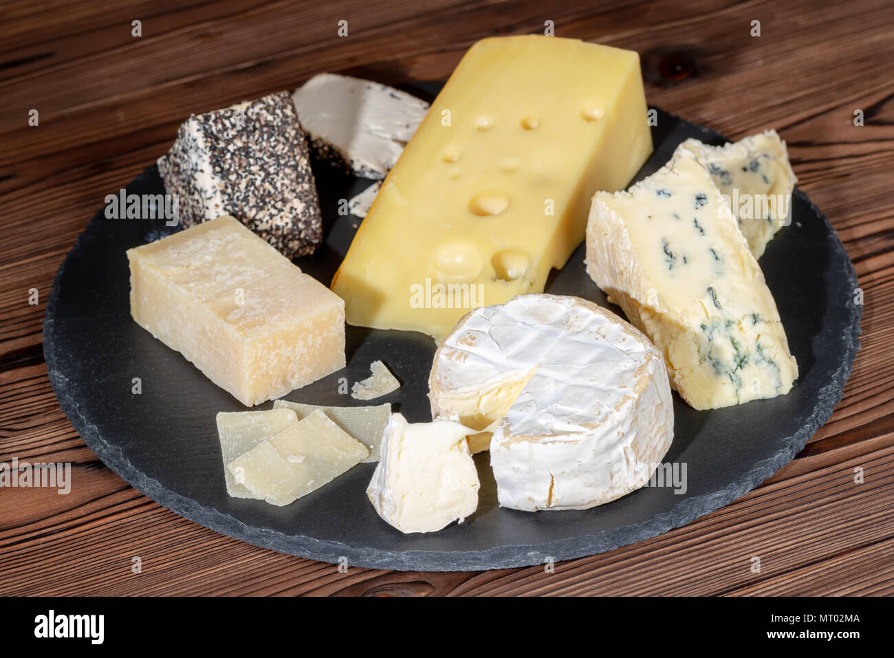 portions various types of fresh cheese on black slate texture, close up ...