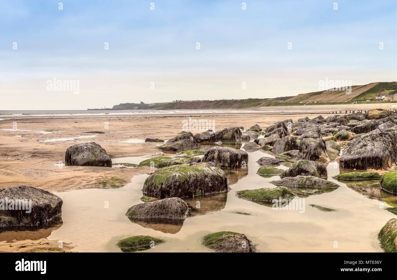 A view of Whitby from a rock strewn beach. A pool of seawater is in the ...