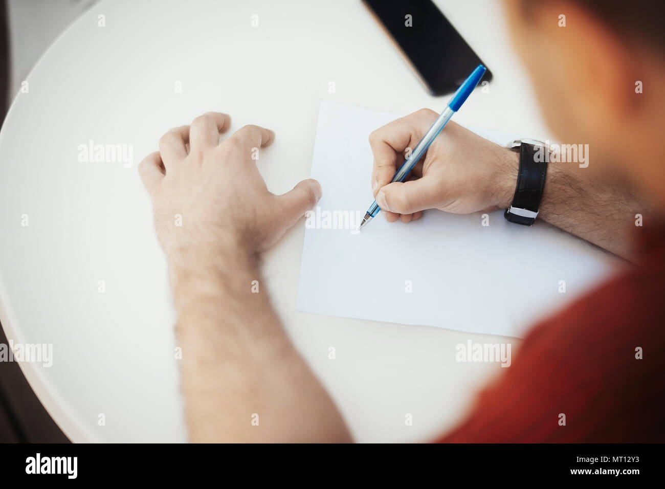 Young attractive man writing note at the paper. Man is on foreground ...