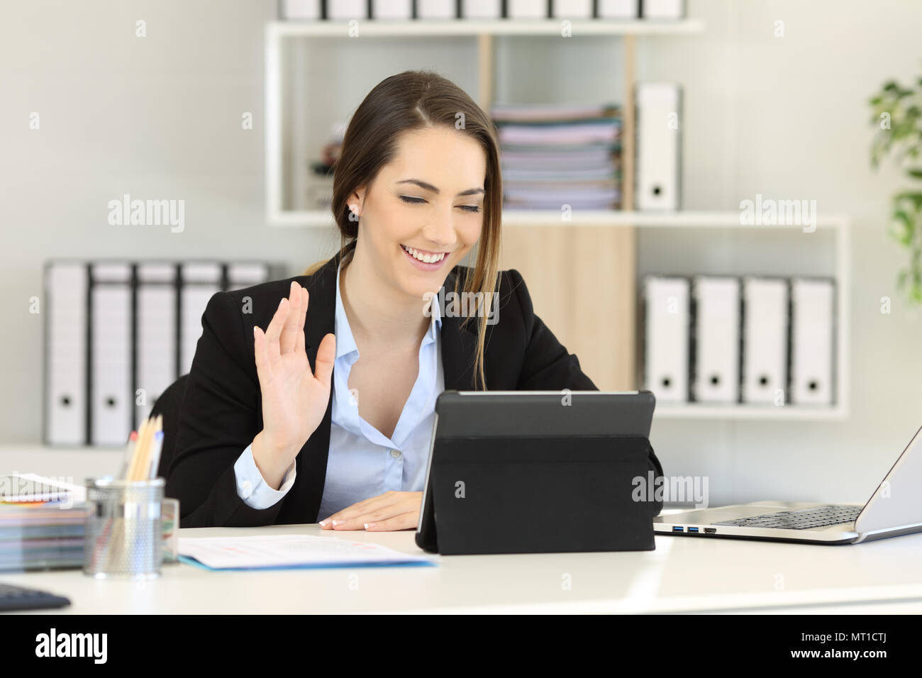 Happy office worker waving in a video conference with a tablet on a ...