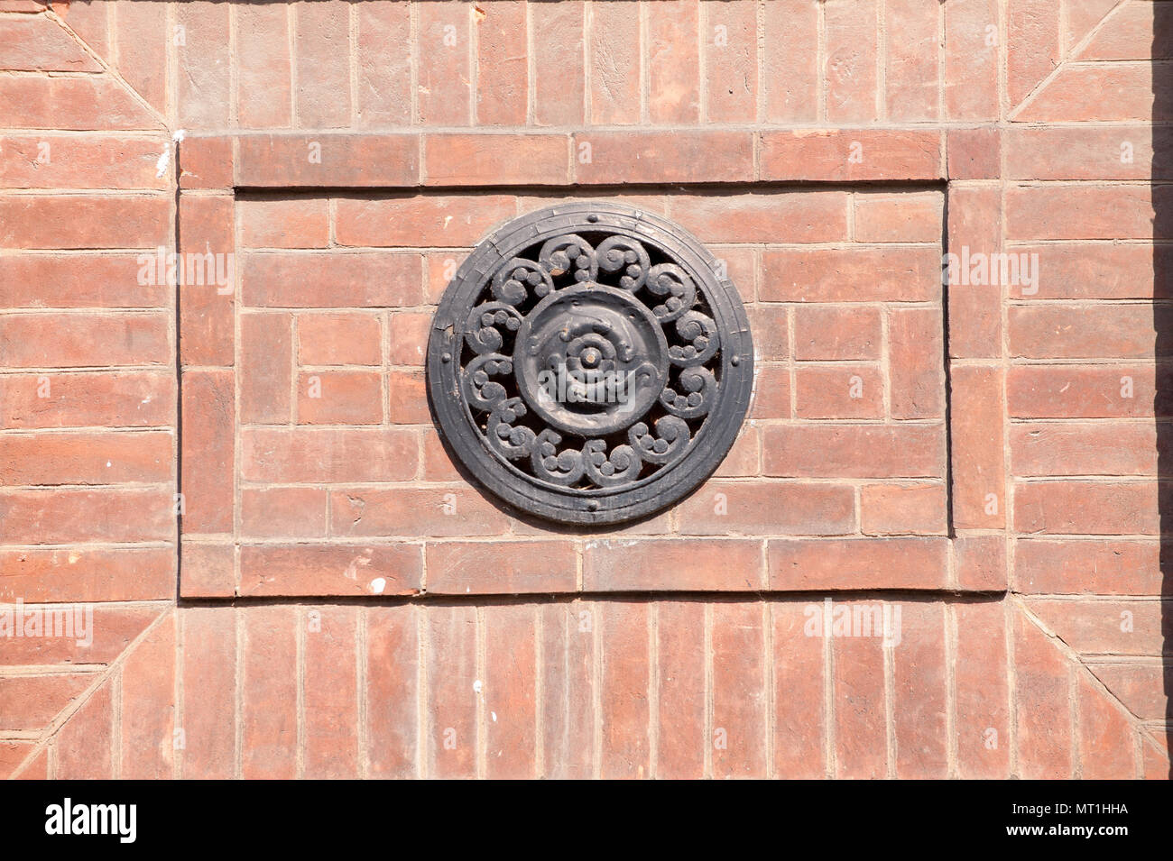 Decorative black cast iron roundel set into red brickwork on a historic ...