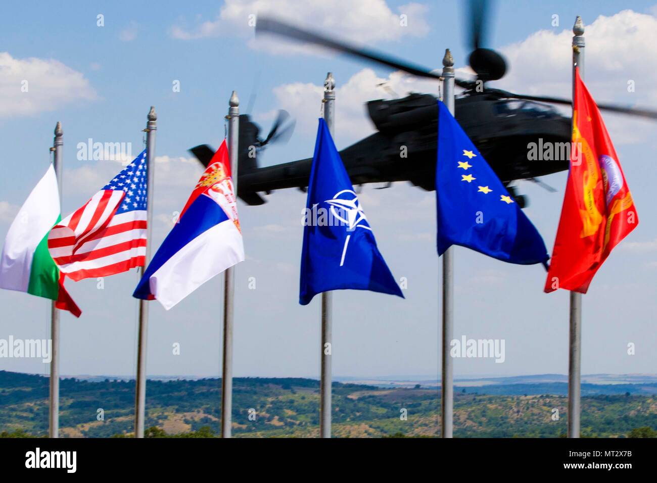 An AH-64 Apache helicopter flies low behind a line of flags during a ...