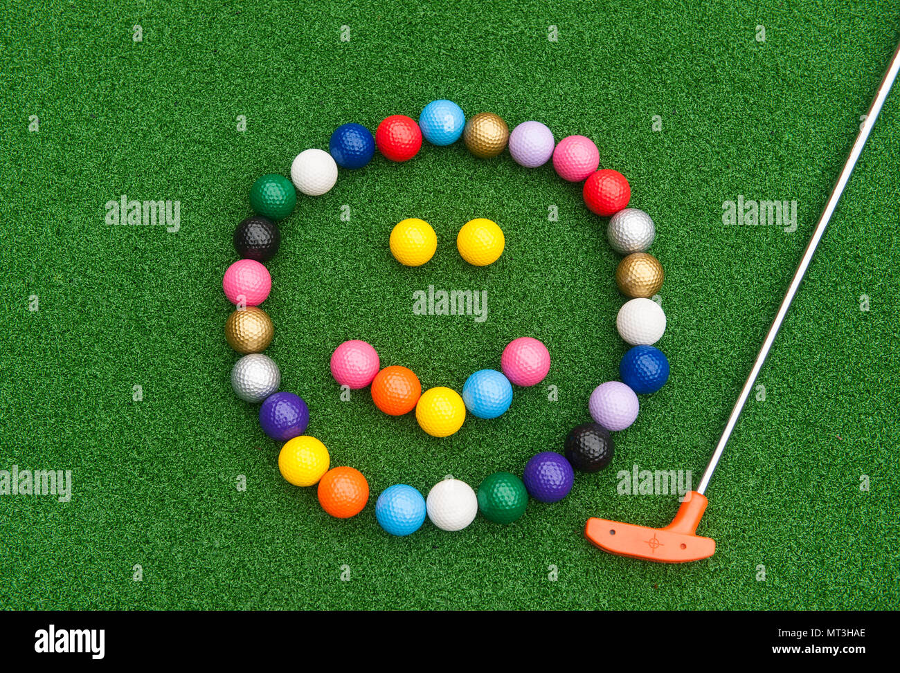 Colorful mini golf ball happy face with orange putter on synthetic ...