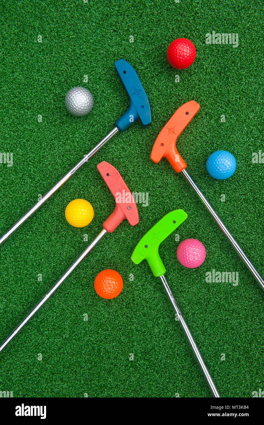 Miniature golf balls and putters in assorted colors on artificial grass ...