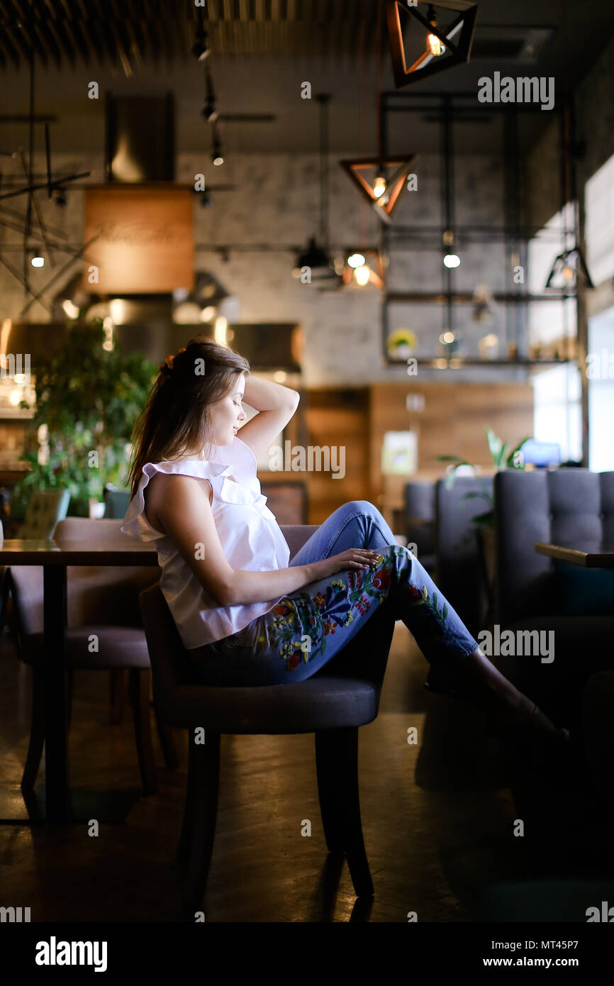 Caucasian photo model sitting at cafe with feet on back of chair ...