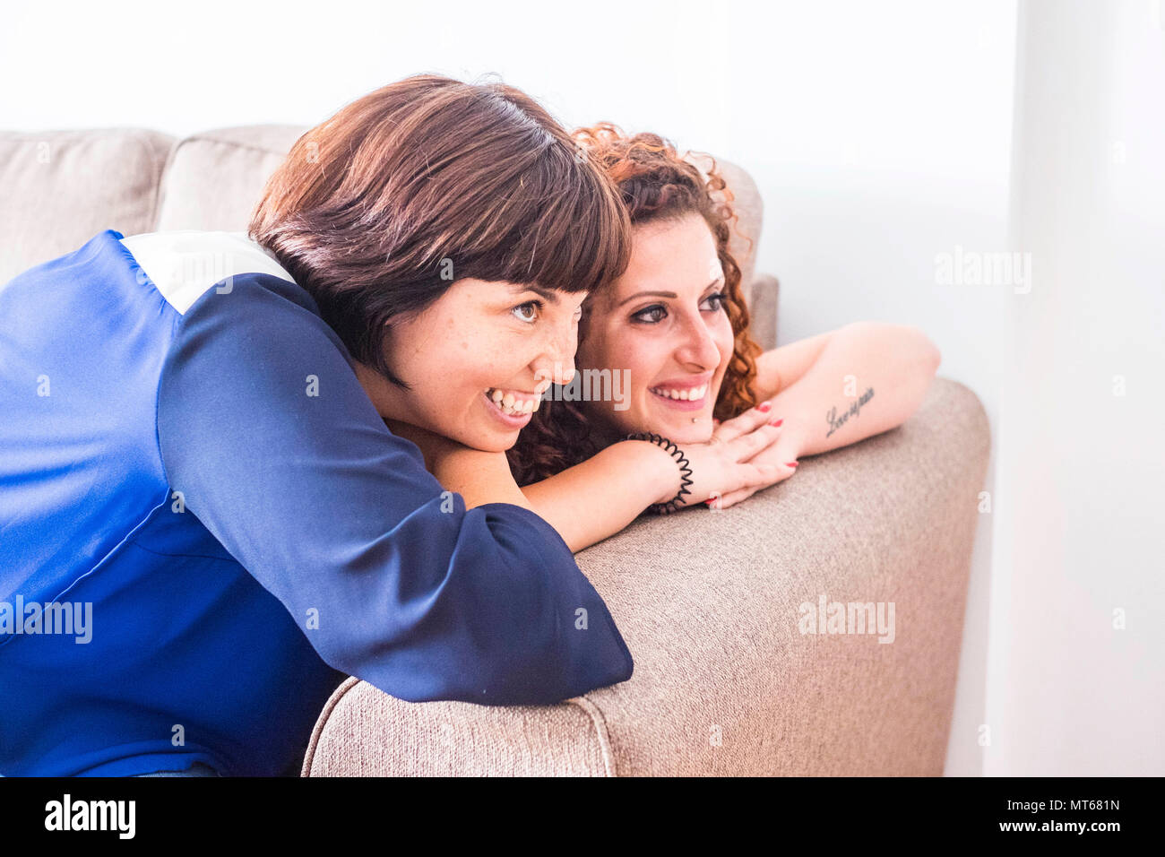 couple od two women friends stay close together on the sofa smiling and ...