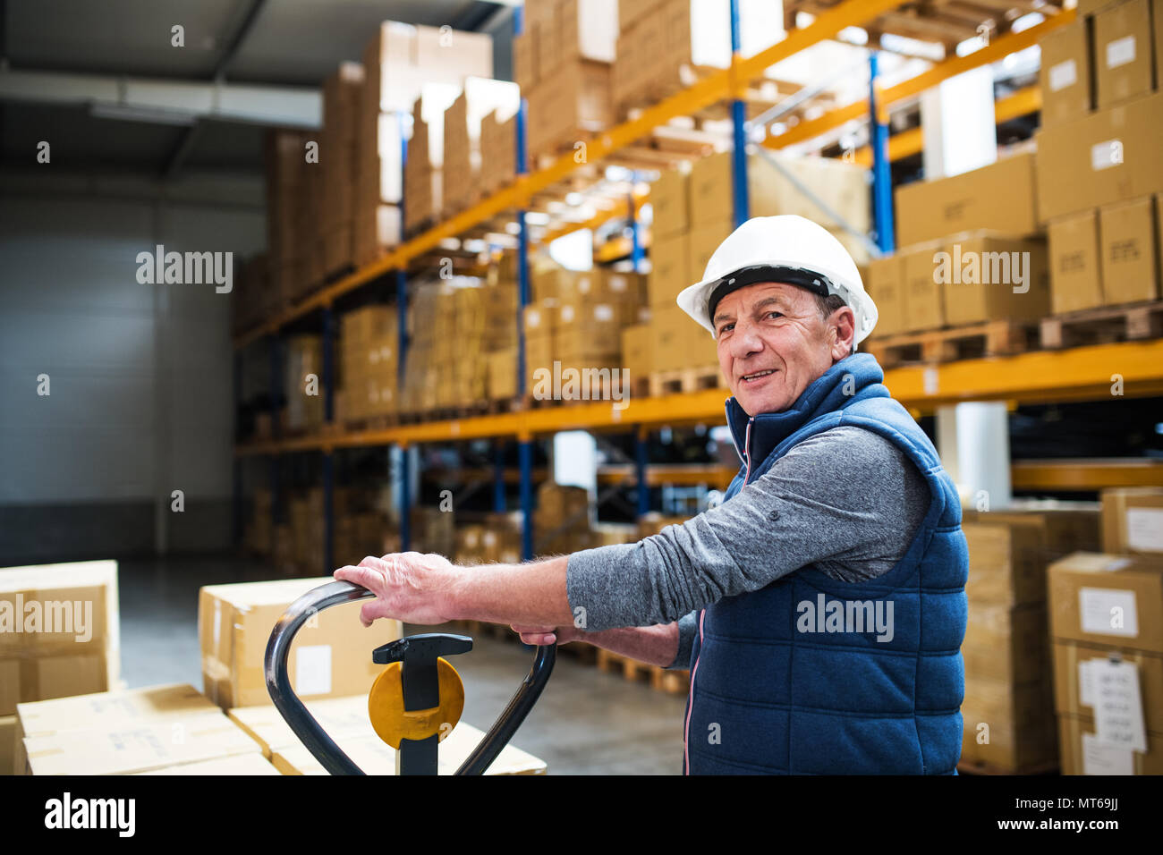 Senior male warehouse worker or a supervisor pulling a pallet truck ...