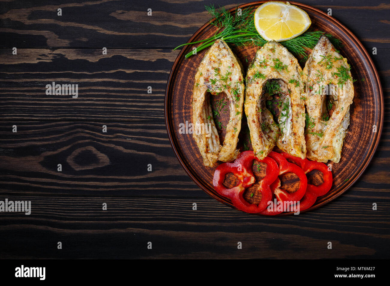 Fried fish in clay plate, on dark wooden background Stock Photo - Alamy