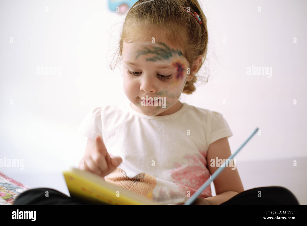 Young child girl reading a book. Face-painting and smile. Empty copy ...