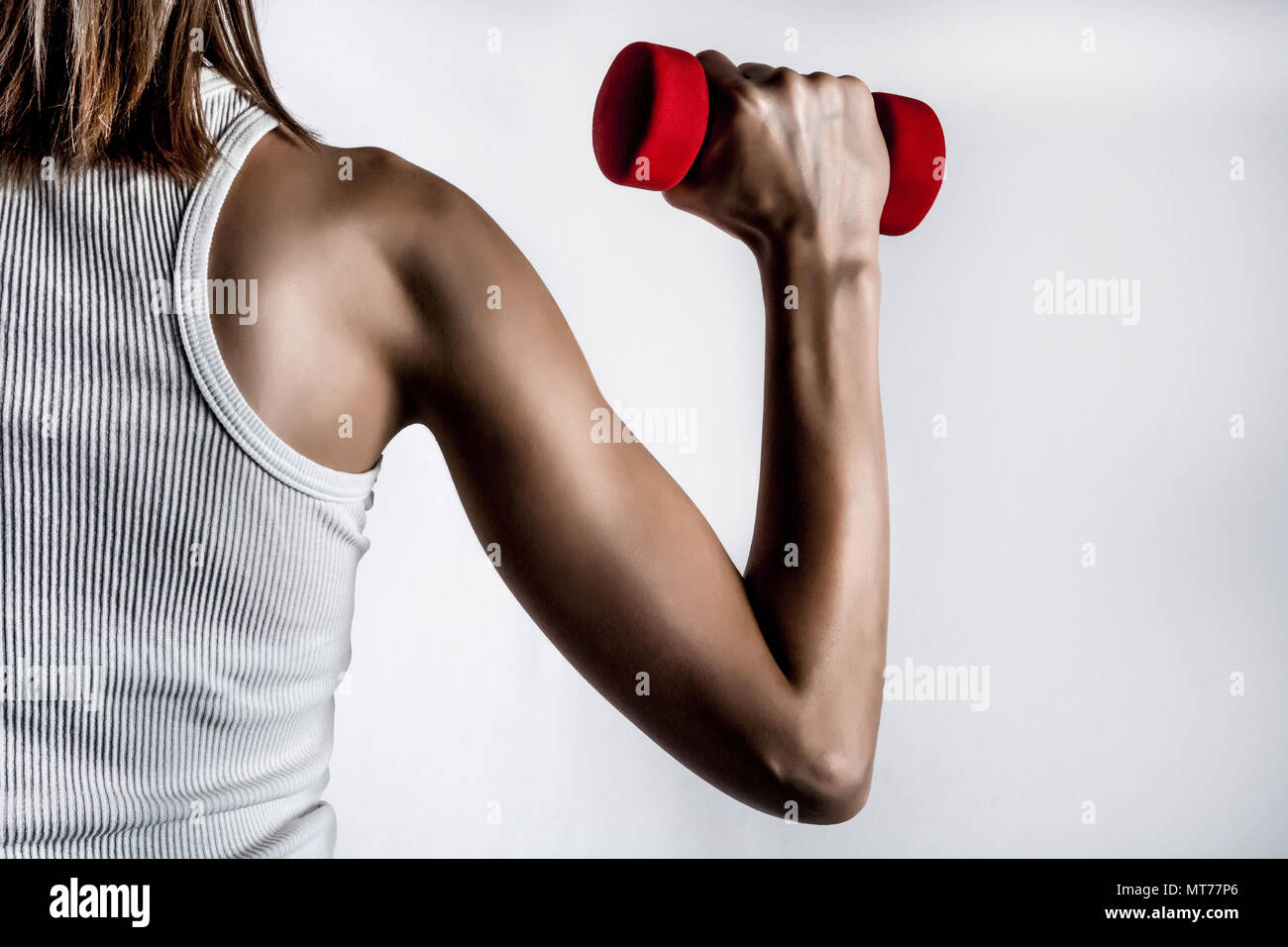 Female back and muscle hand with dumbbell in t shirt in gray studio ...