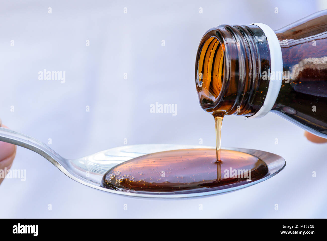 Hand pouring medication or antipyretic syrup from bottle to spoon ...