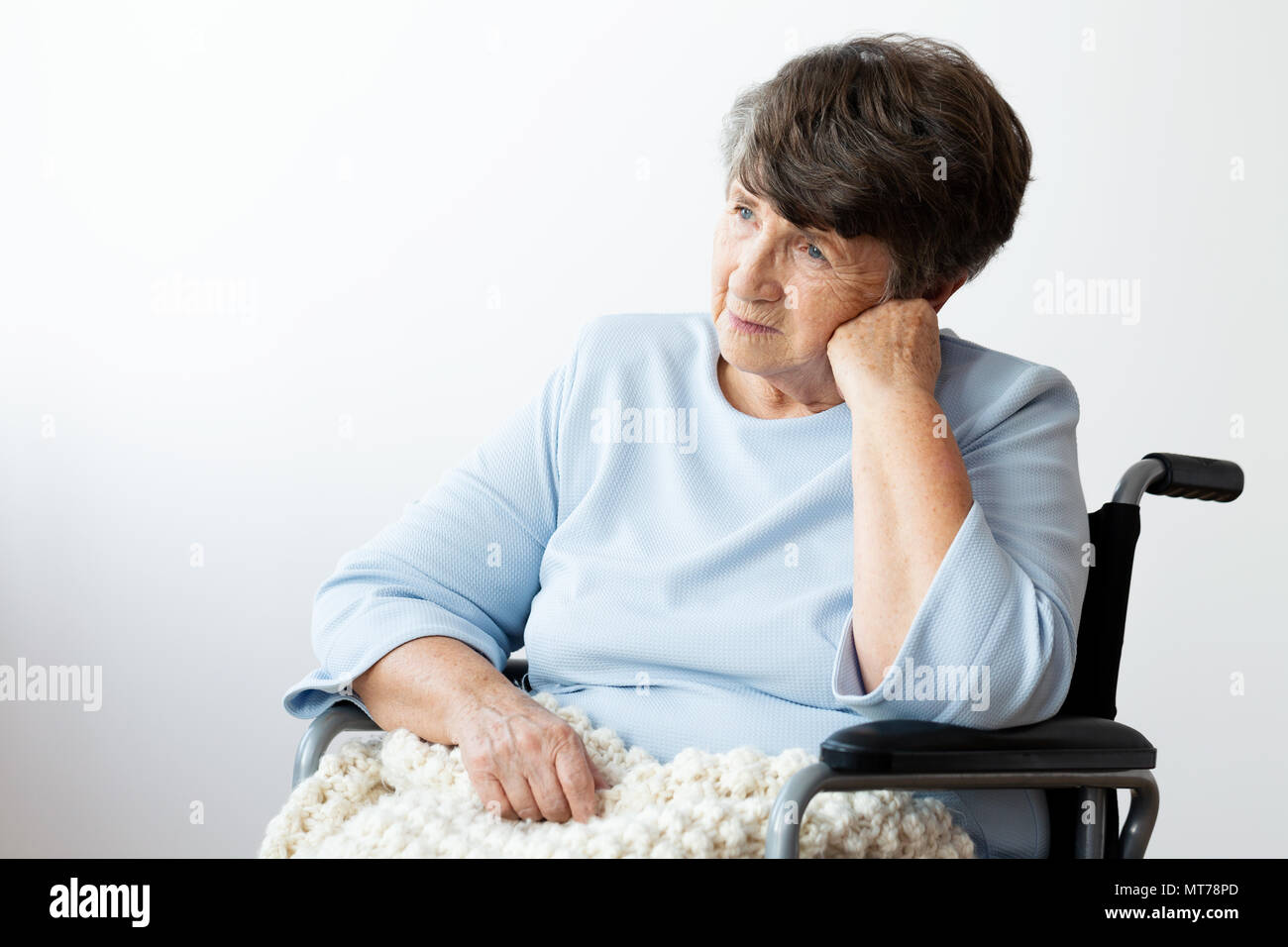 Sad disabled senior woman in a wheelchair against white background ...