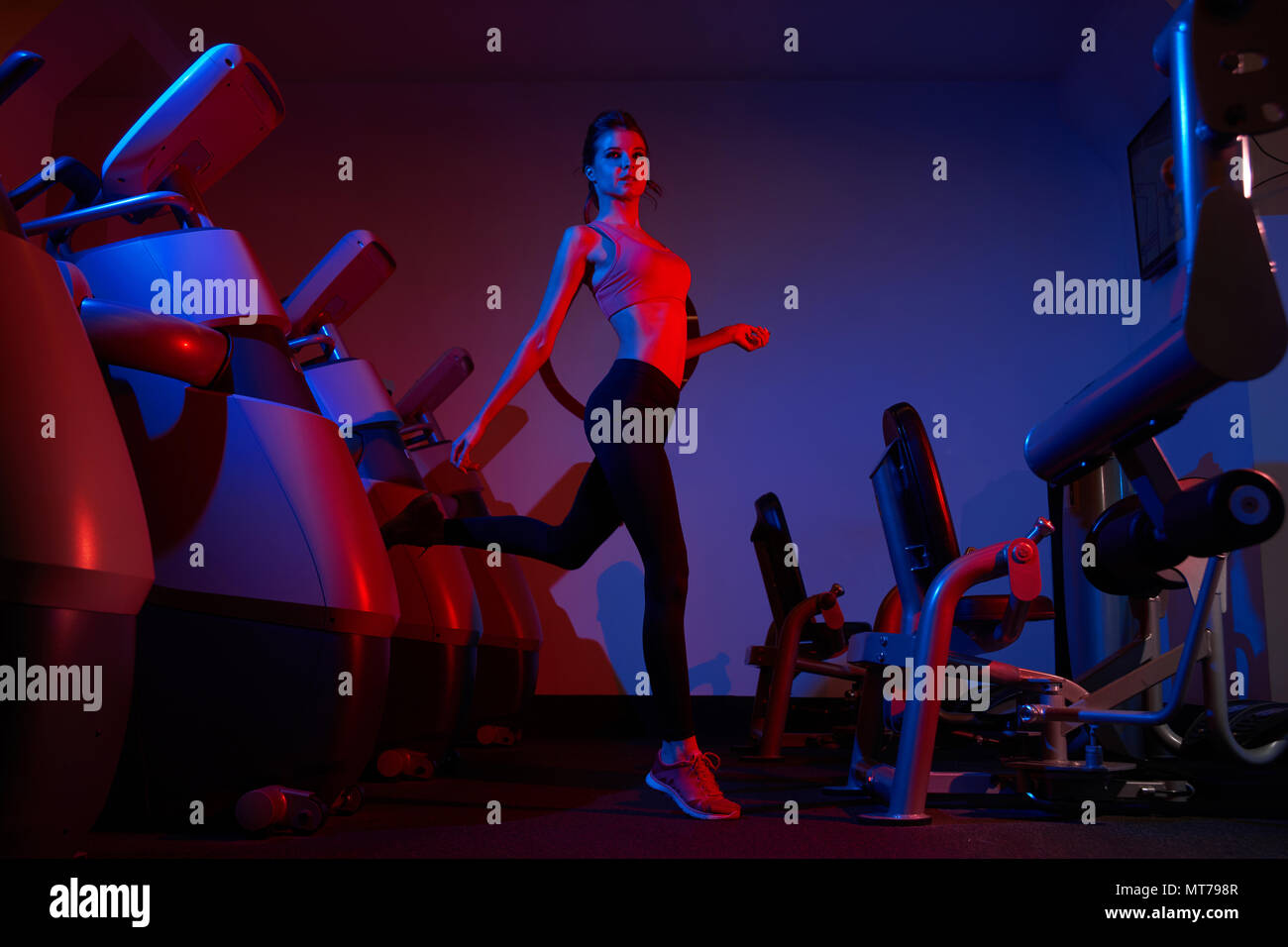 Slim woman jumping between rows of exercise machines Stock Photo - Alamy