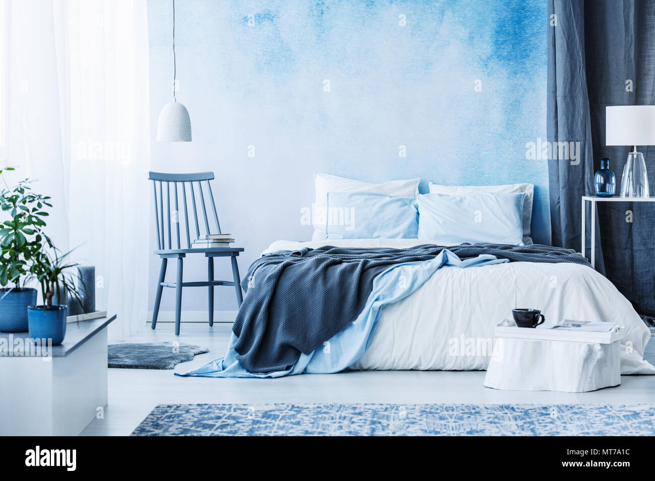 Blue chair next to bed with grey blanket in cozy bedroom interior with ...