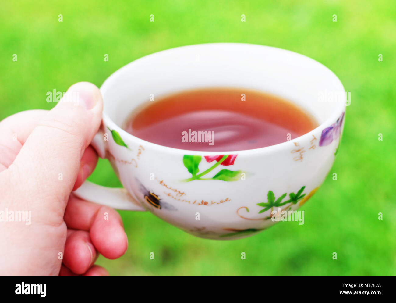 Cup of tea in hand on green summer background Stock Photo - Alamy