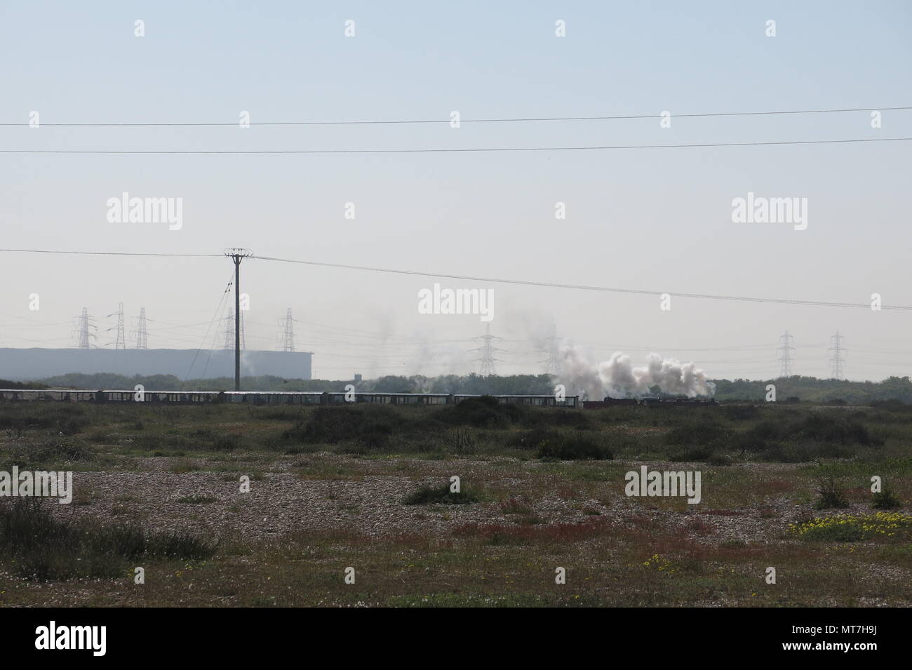 A steam train roars by in a cloud of smoke, past the Dungeness Power ...