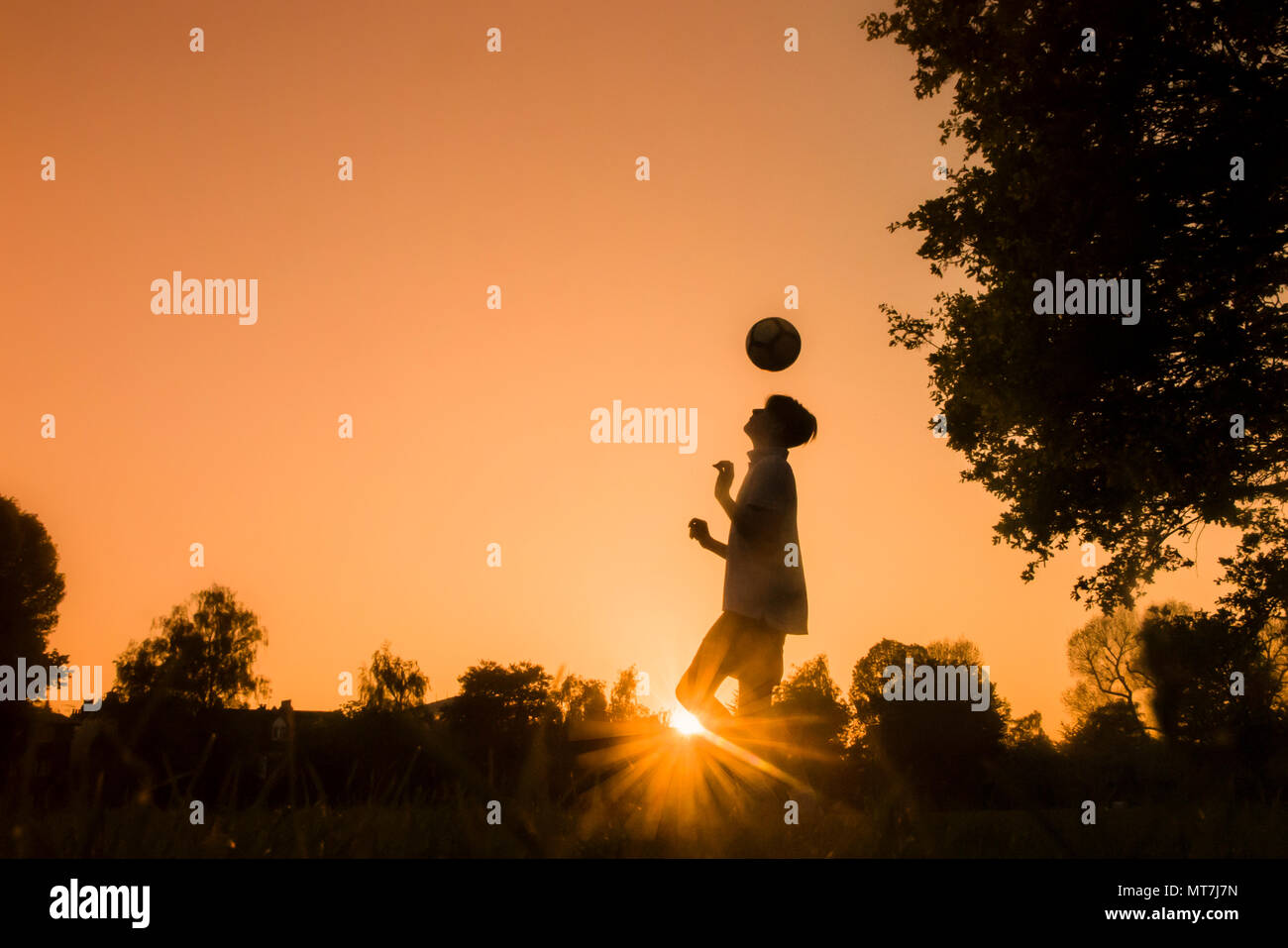 A boy playing football as the sun goes down on a summer's evening Stock ...