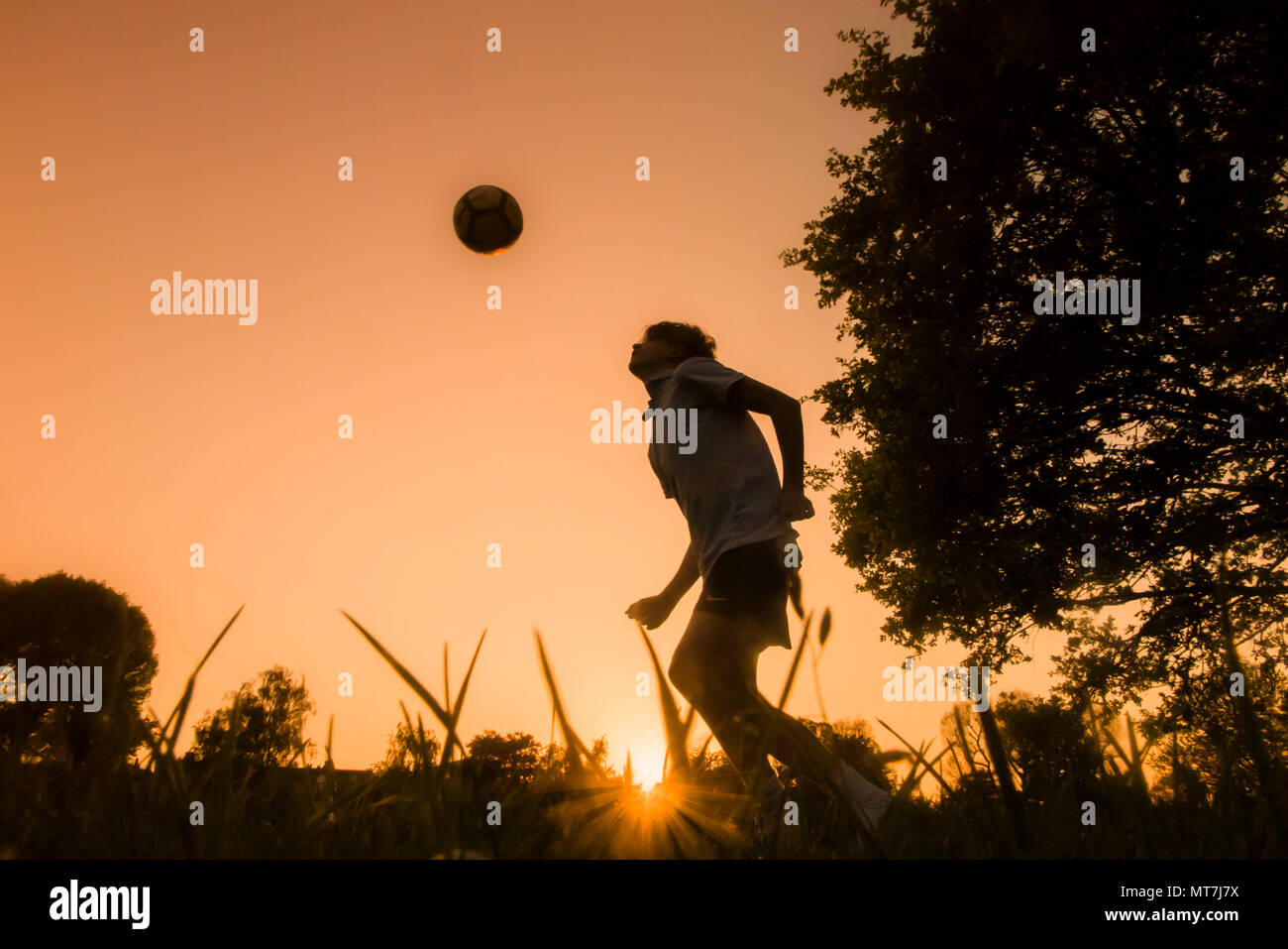 A boy playing football as the sun goes down on a summer's evening Stock ...