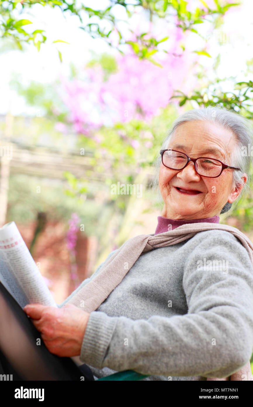 one senior asian woman reading book in the yard and smile at camera ...