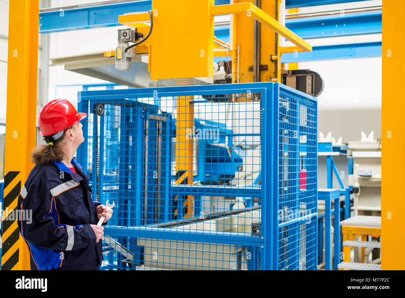 Worker in a factory wearing blue working suit and red helmet looking up ...