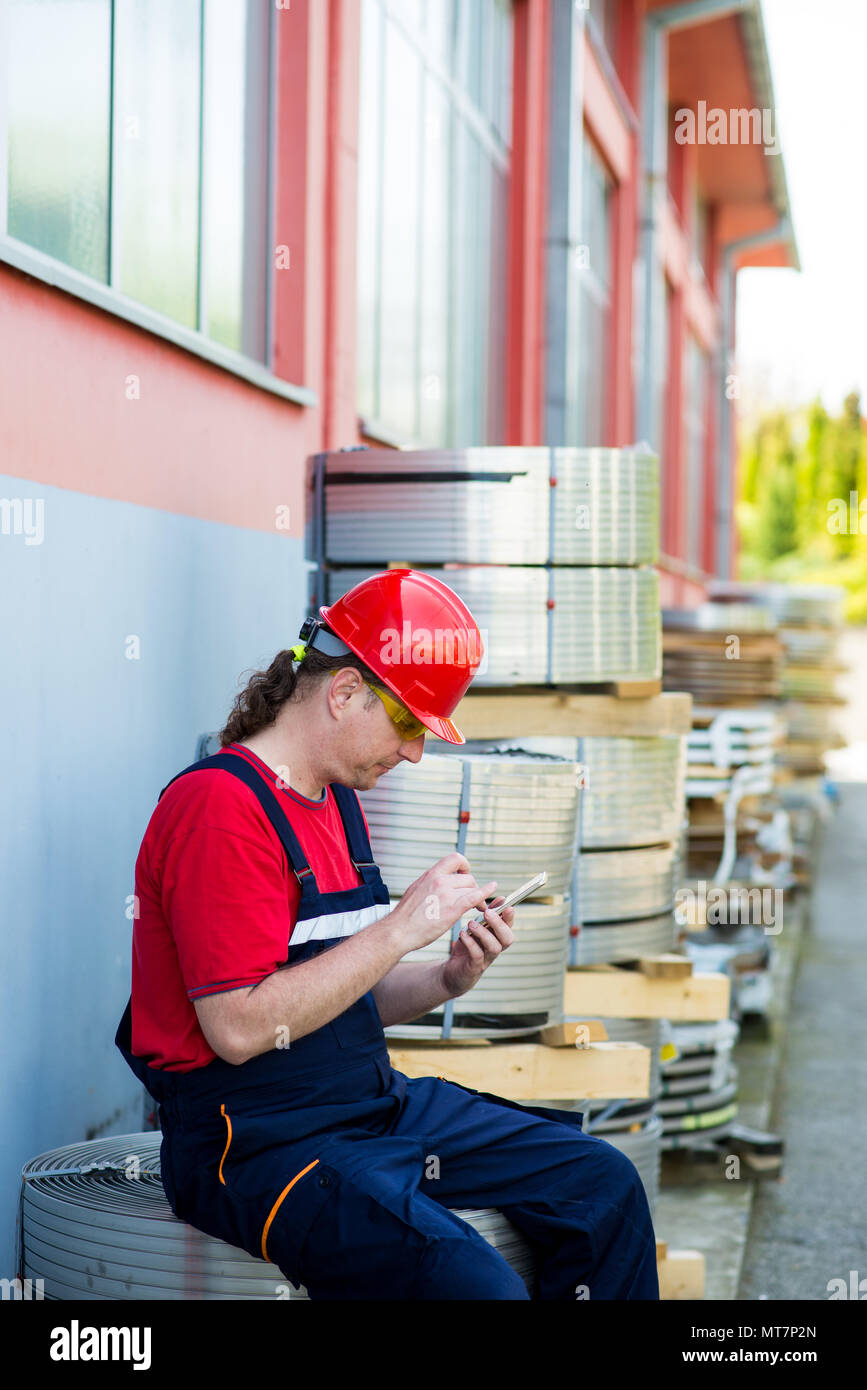 Worker using his mobile phone and relaxing outside a factory. Worker ...