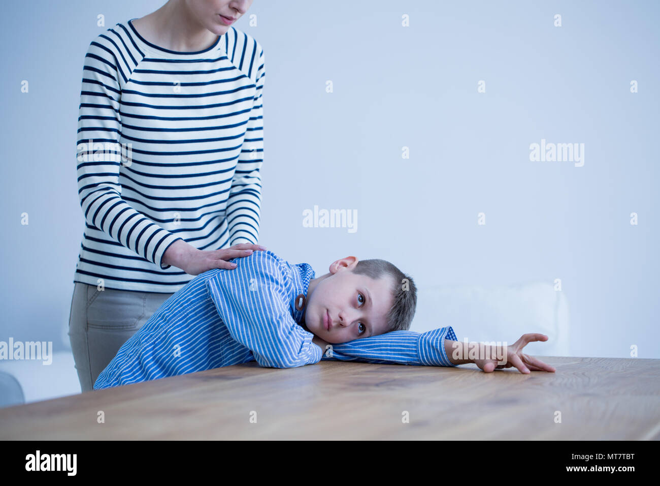 Sad autistic boy lying on a table and his mother standing next to him ...