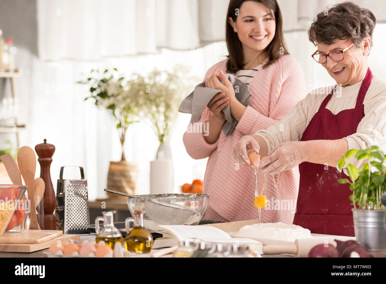 Happy grandma cracking an egg and cooking in a kitchen with her ...