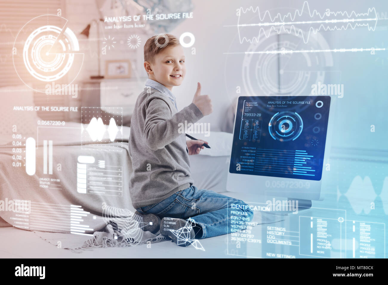 Happy child putting his thumb up while sitting in front of his computer ...