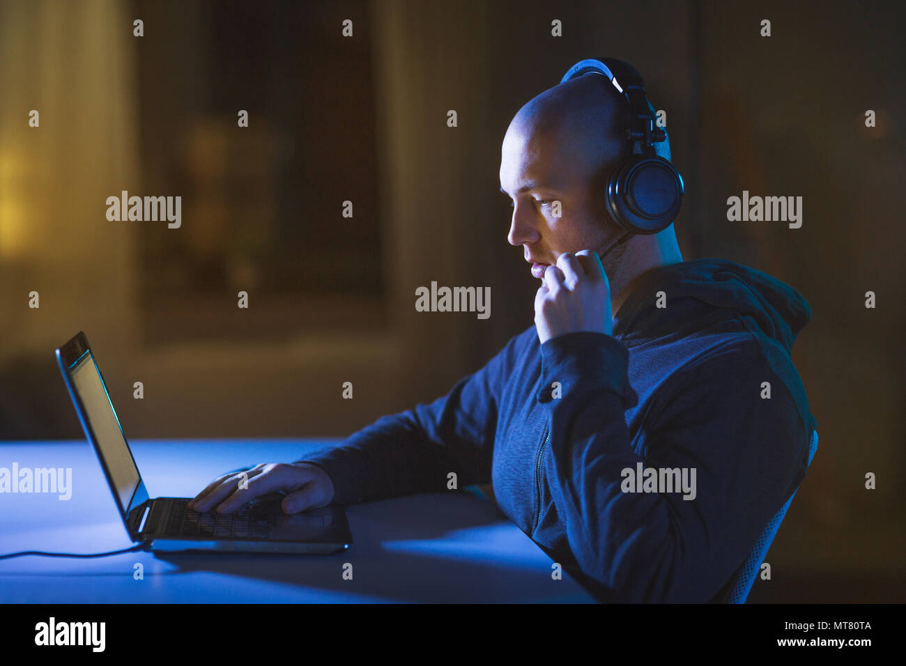 hacker in headset typing on laptop in dark room Stock Photo - Alamy