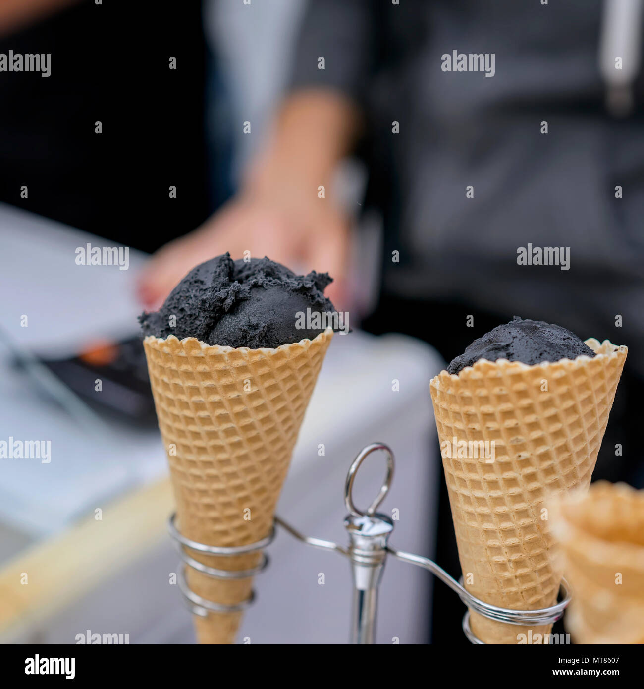 Two waffle cones, horns with balls of trendy black ice cream and hand ...