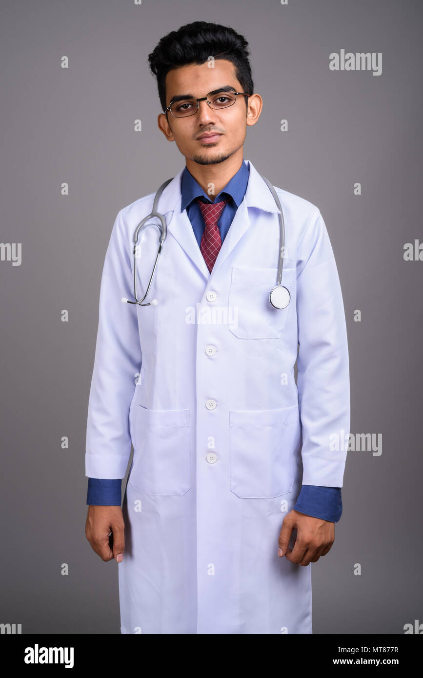 Young Indian man doctor against gray background Stock Photo - Alamy