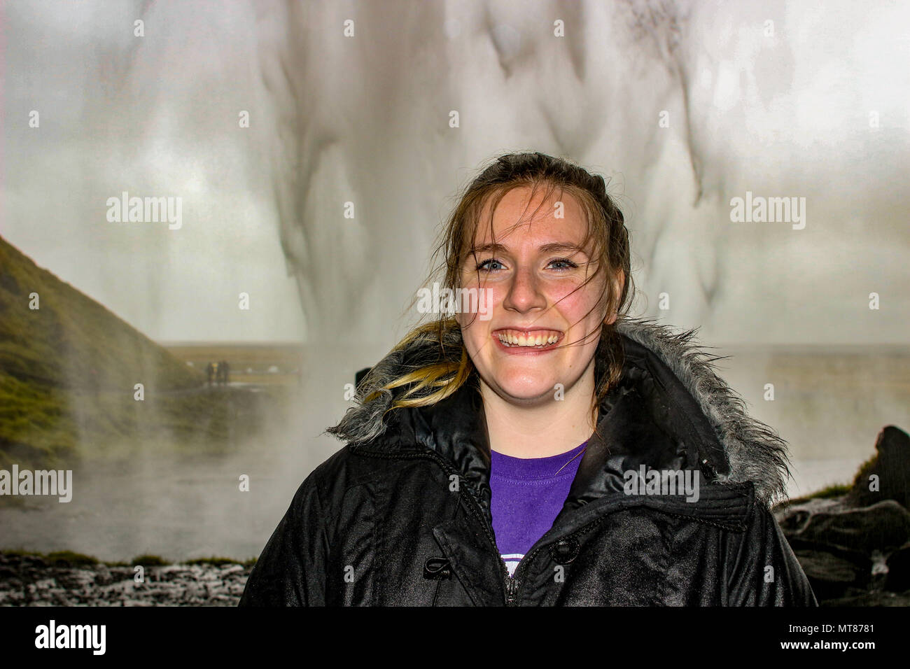 Young tourist, 20 to 25 years old poses behind a waterfall in Iceland ...