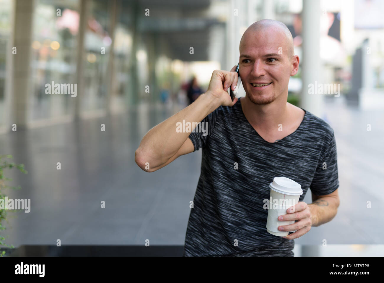 Thoughtful young happy bald man smiling and holding paper coffee Stock ...