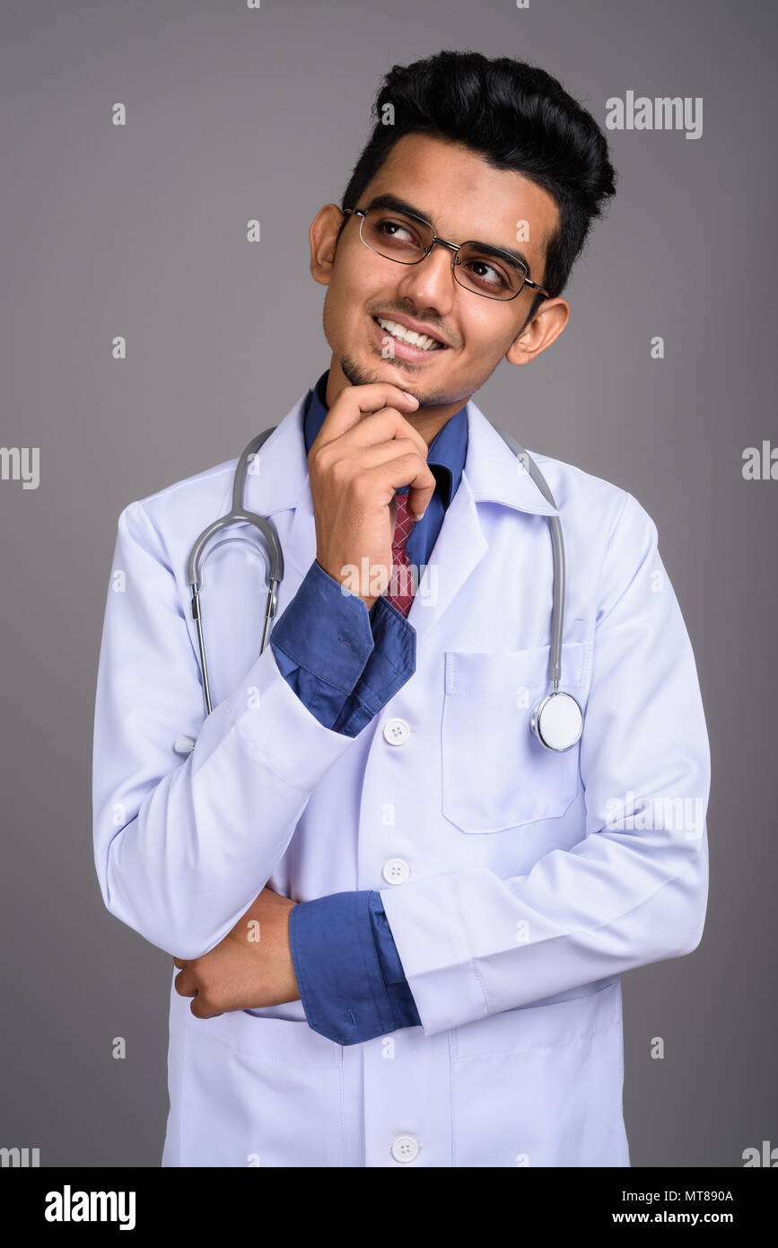 Young Indian man doctor against gray background Stock Photo - Alamy