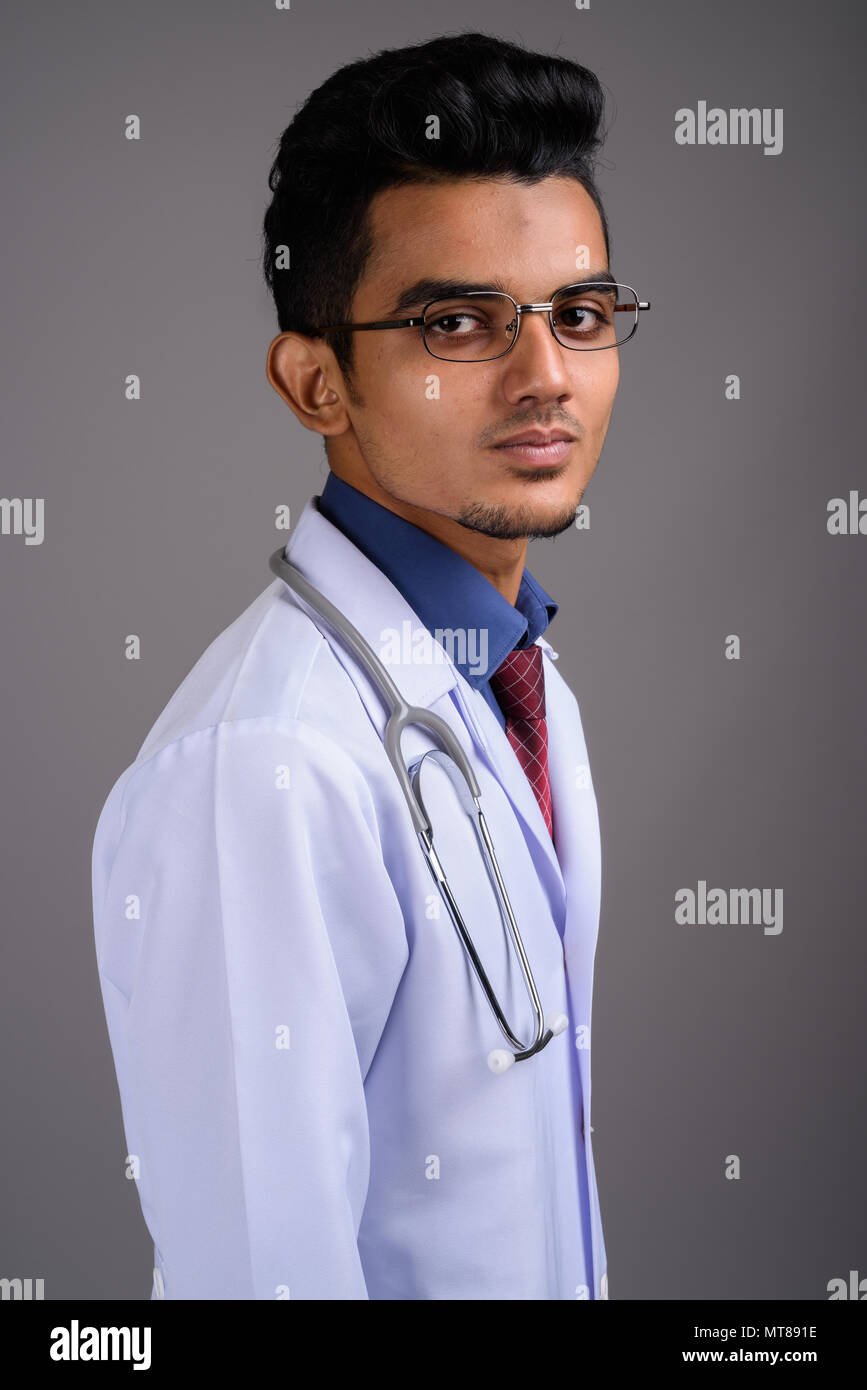 Young Indian man doctor against gray background Stock Photo - Alamy