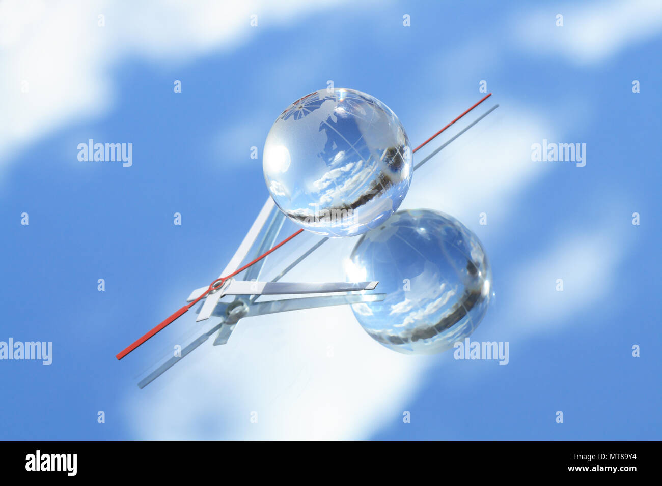 Glass glode and clock hands lying on mirror background with blue sky ...