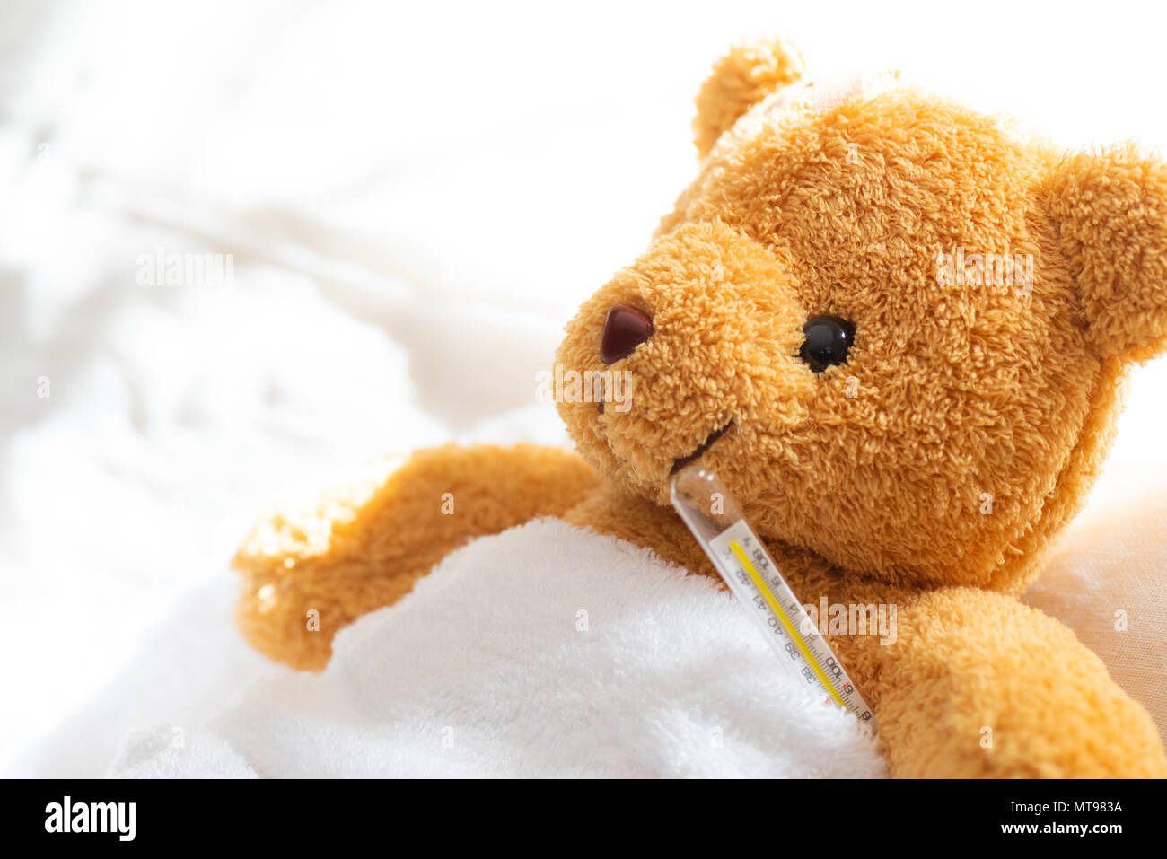 Teddy bear lyiing sick in hospital bed with with thermometer and ...