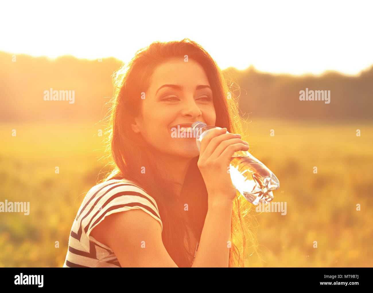 Happy smiling woman drinking water from the bottle on summer bright ...