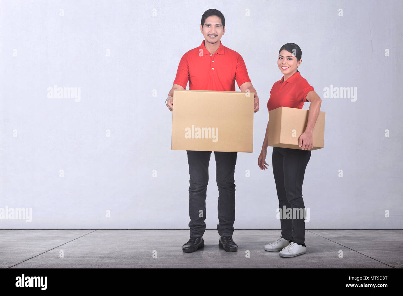 Attractive asian delivery service team with cardboards box over wall ...